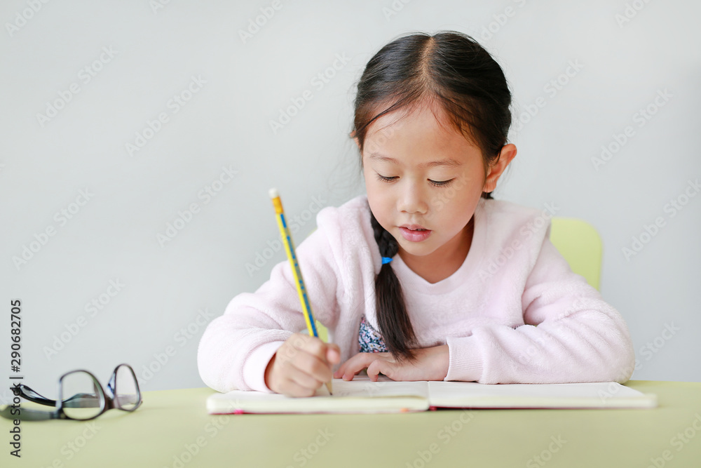 Portraits of little Asian child girl write in a book or notebook with ...