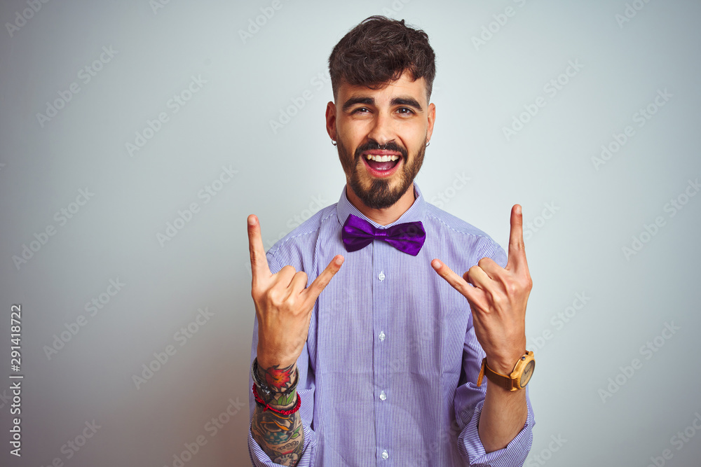 Young man with tattoo wearing purple shirt and bow tie over isolated ...