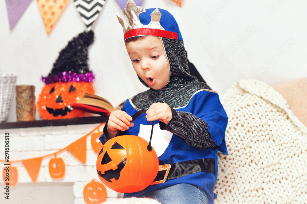 Little surprised boy in a knight costume with a crown on his head sits ...