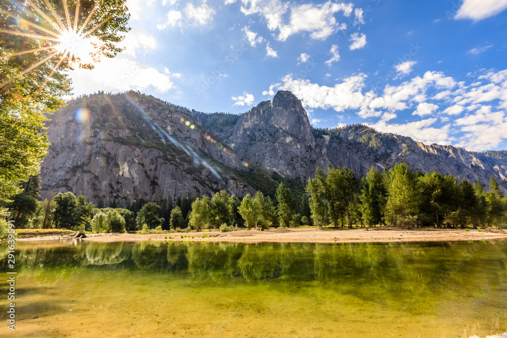 A sunburst in the left corner highlights lush trees and Sentinel Rock ...