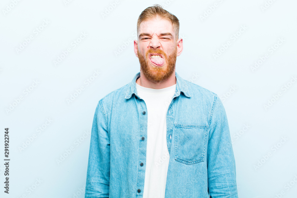 young red head man feeling disgusted and irritated, sticking tongue out ...