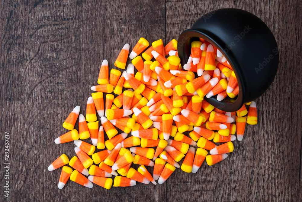 Black ceramic cauldron filled with holiday candy corn tipped over on a ...