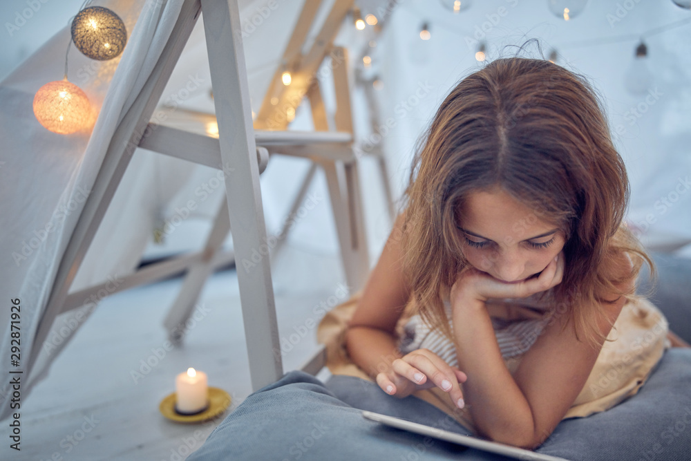 Little 10 year old girl using tablet under her home-made tent inside ...