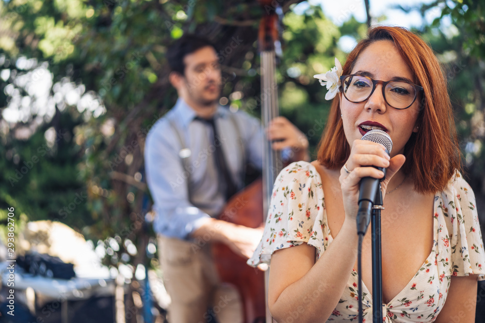 female jazz singer singing on stage with a bass player behind outdoors ...