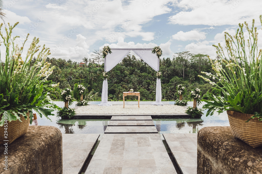 White Wedding ceremony arch in tropical jungle on edge of blue infinity ...