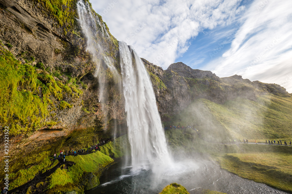 Seljalandsfoss waterfall drops from cliffs that allow people to walk ...
