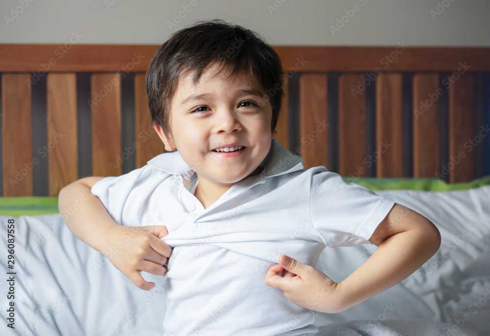 School boy sitting in bed and try to wearing his cloth with smiling ...