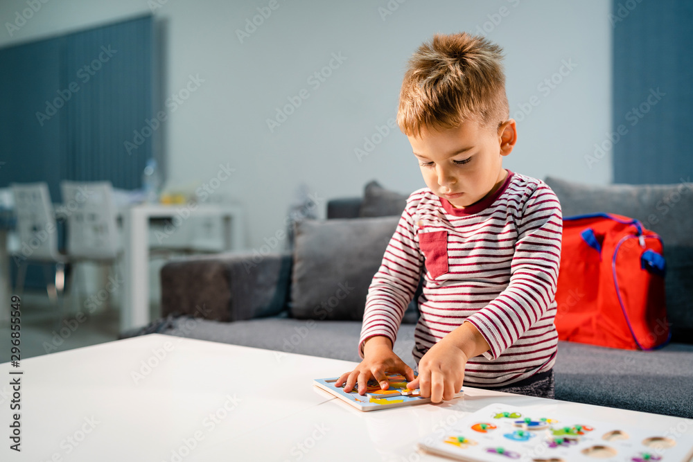 Small boy little playing at home alone by the table with puzzle ...