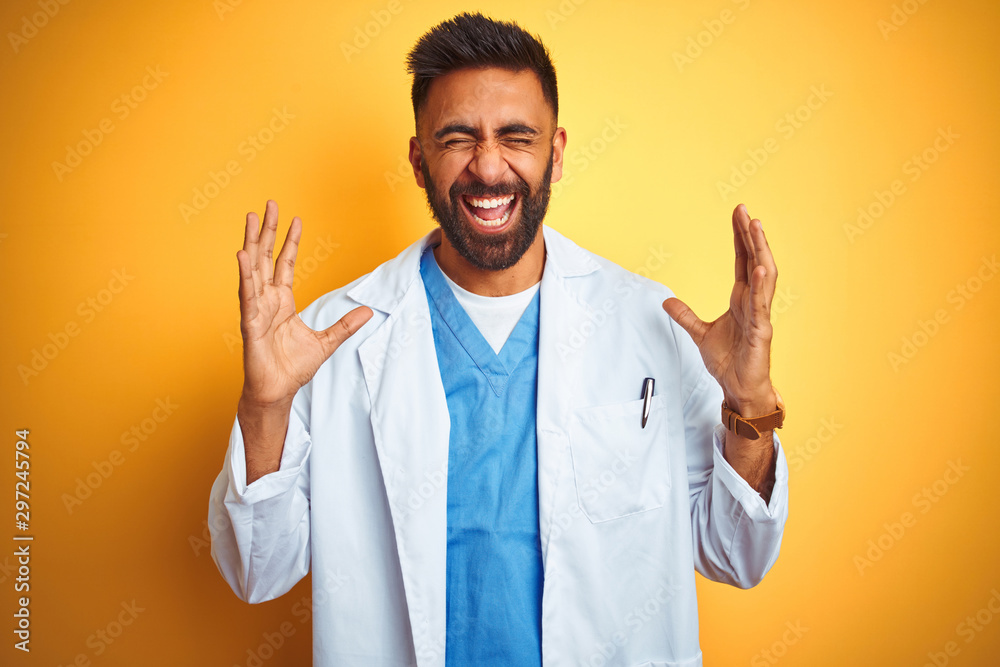 Young indian doctor man standing over isolated yellow background ...