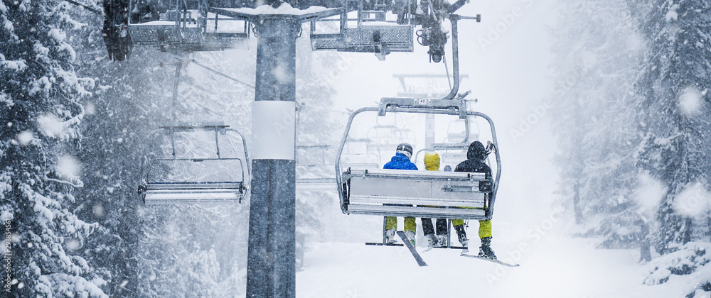 Three skiers on ski lift in heavy snowing storm. Beautiful vacation in ...