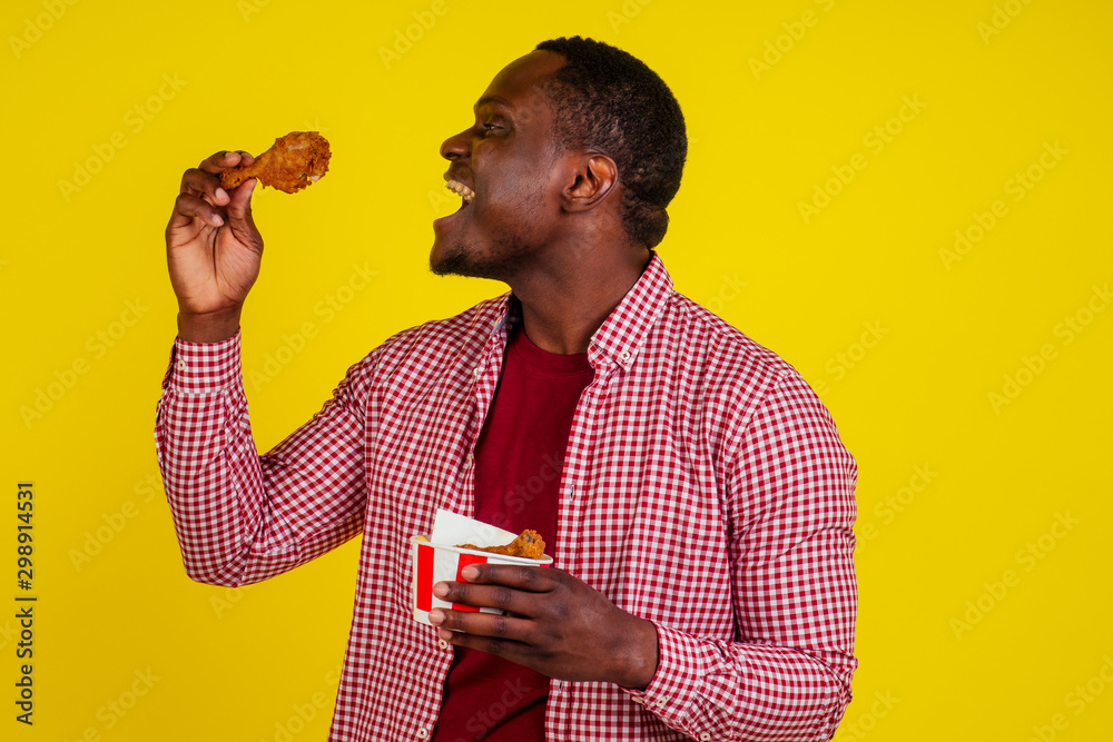 funny african american man eating fried chicken leg in studio yellow ...