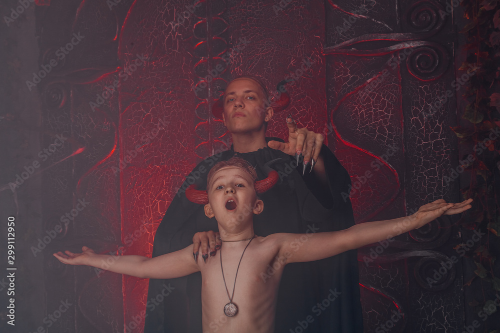 small child with red horns of demon and adult scary man standing in ...