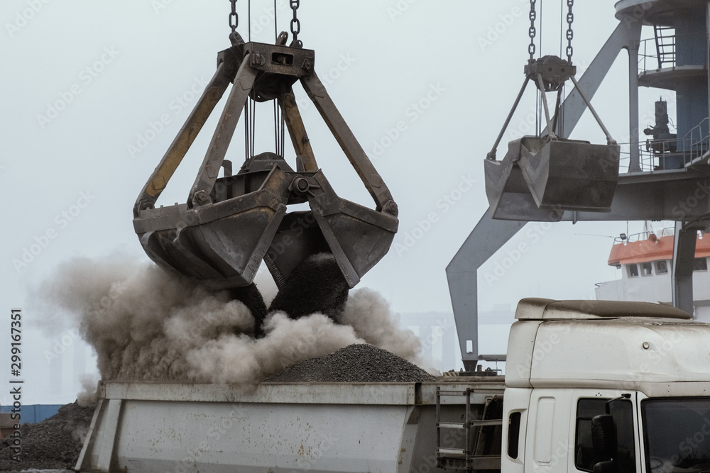 Grapple crane unloading cement clinker from ship to truck in river port ...