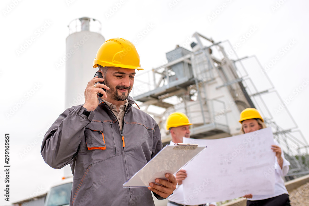 Civil engineer and colleagues on site, wearing safety helmet, checking ...