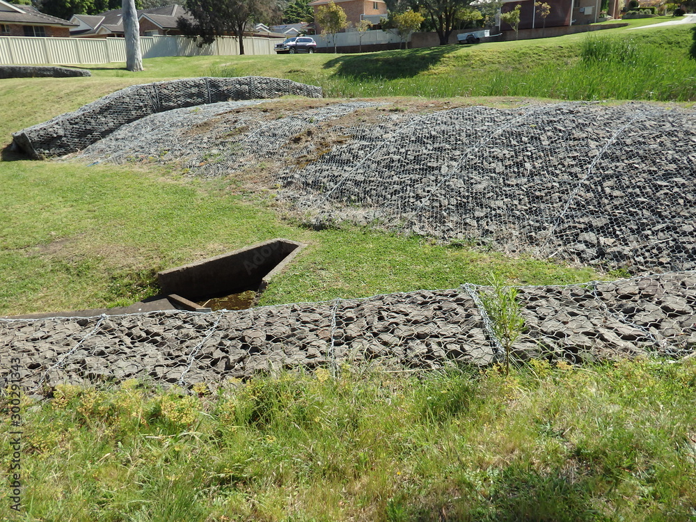 Stone walls under steel mesh creating a spillway for rain water flood ...