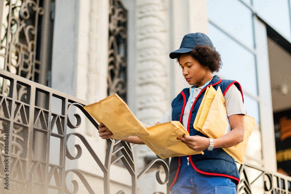 African American delivery woman checking the address on a package ...