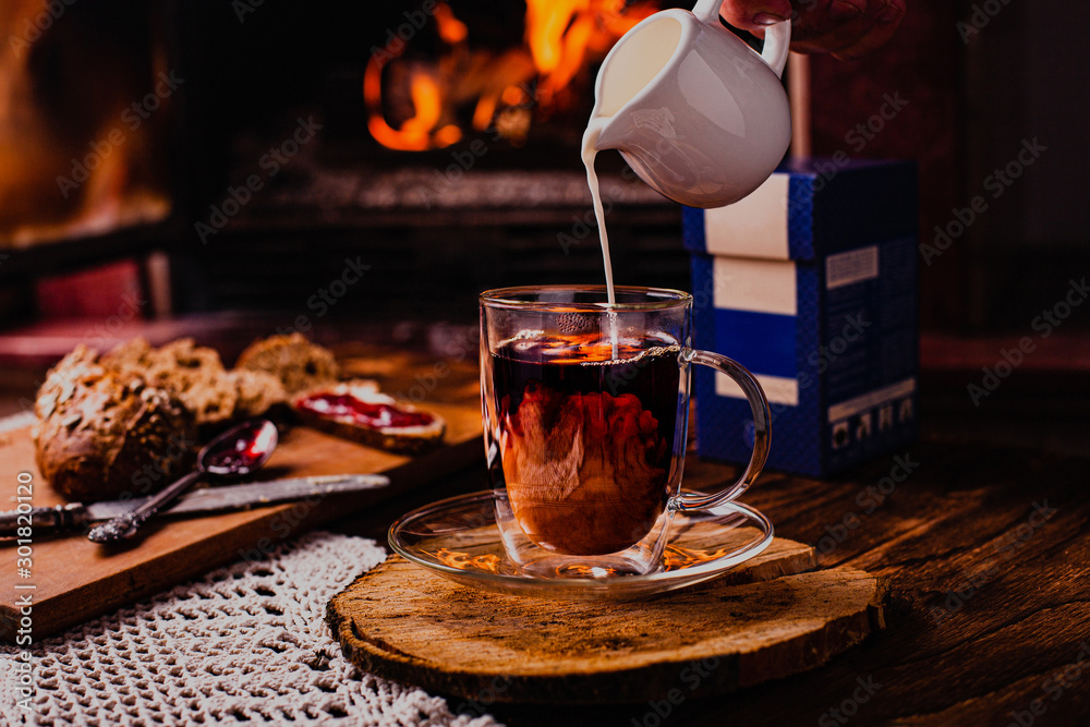 Pouring milk from porcelain milk jug into cup filled with tea - white ...