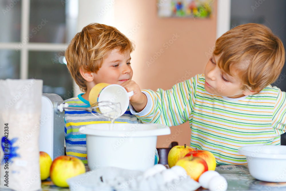 Two little funny brothers baking apple cake in domestic kitchen. Happy ...