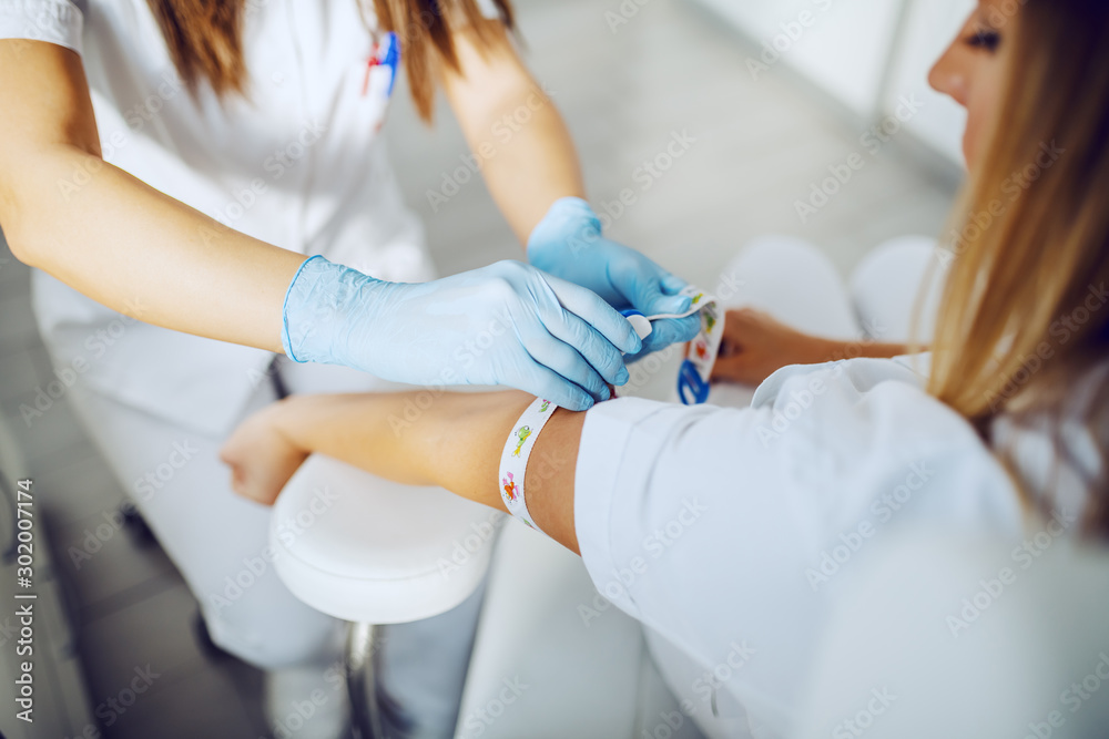 Cropped picture of lab assistant putting band on patient's arm and ...