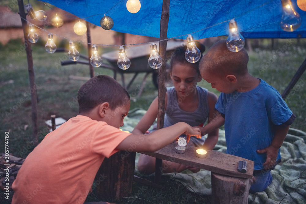 Kids making a small tent with candles and lampions in the backyard ...