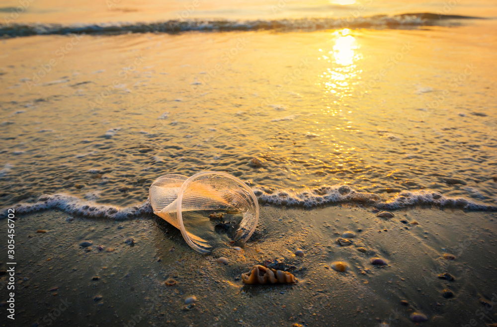 Plastic glass lies on the beach in sunset and pollutes the sea and ...