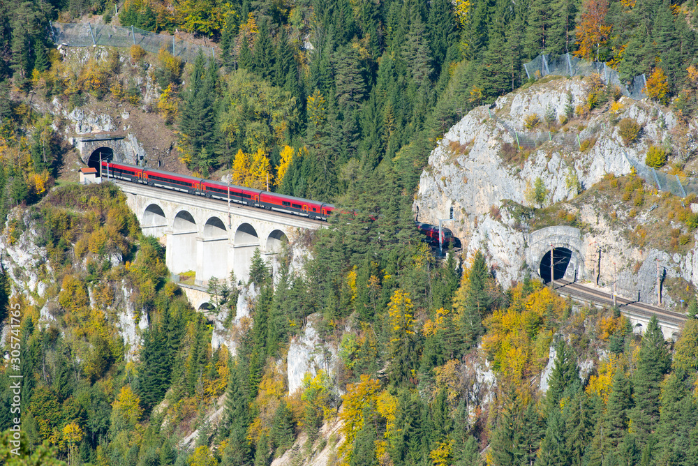 Red train on a viaduct between two tunnels on the Semmering Railway ...