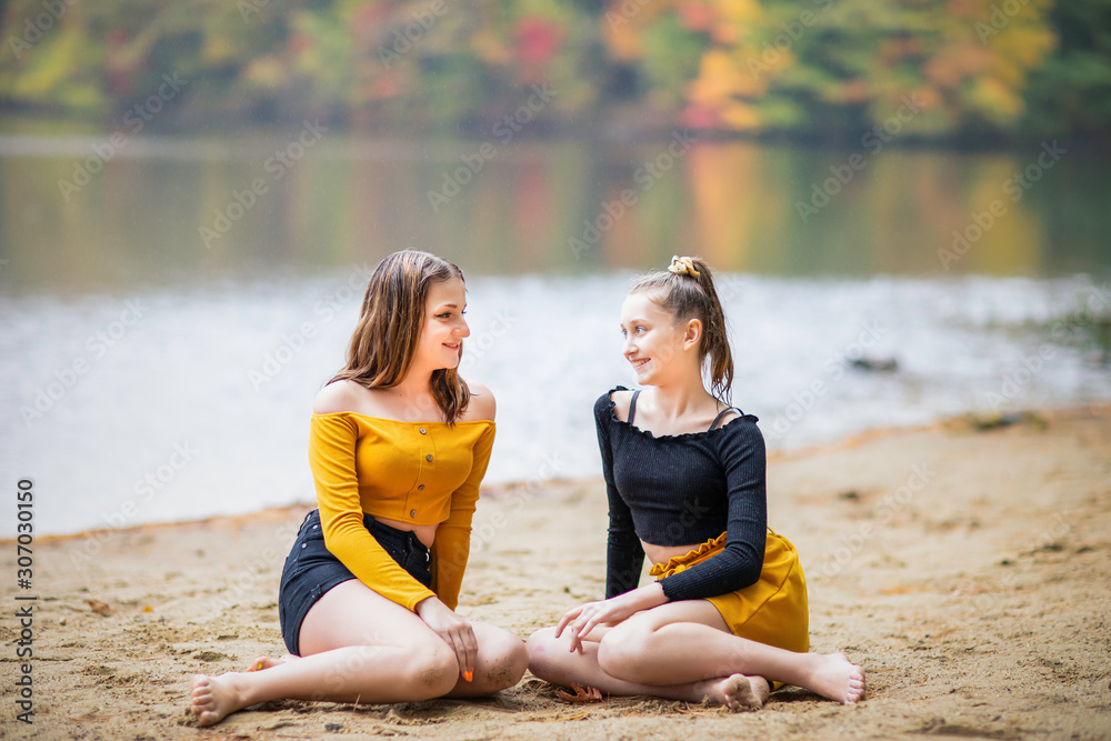 Two beautiful girl teenagers friends, sisters sitting on the beach ...