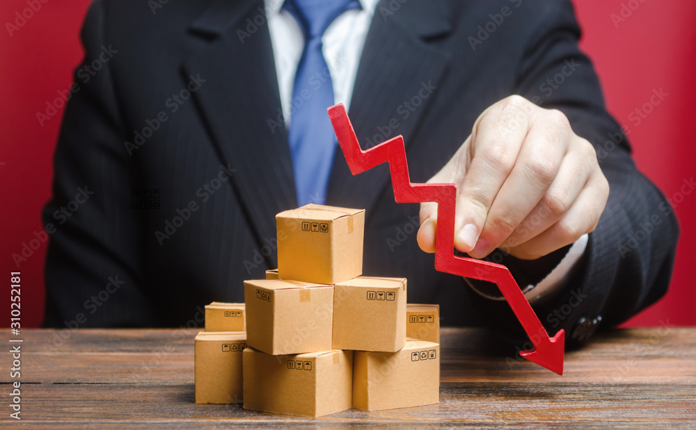 Businessman is holding a red arrow down above boxes stack pile ...