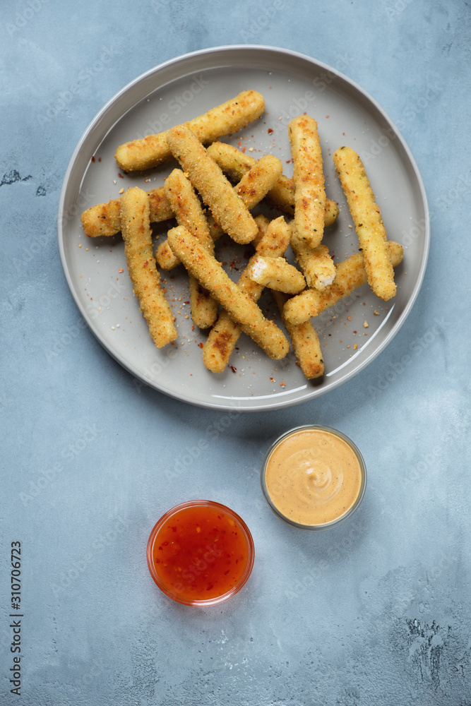 Plate of breaded chicken sticks with dipping sauces over grey concrete ...