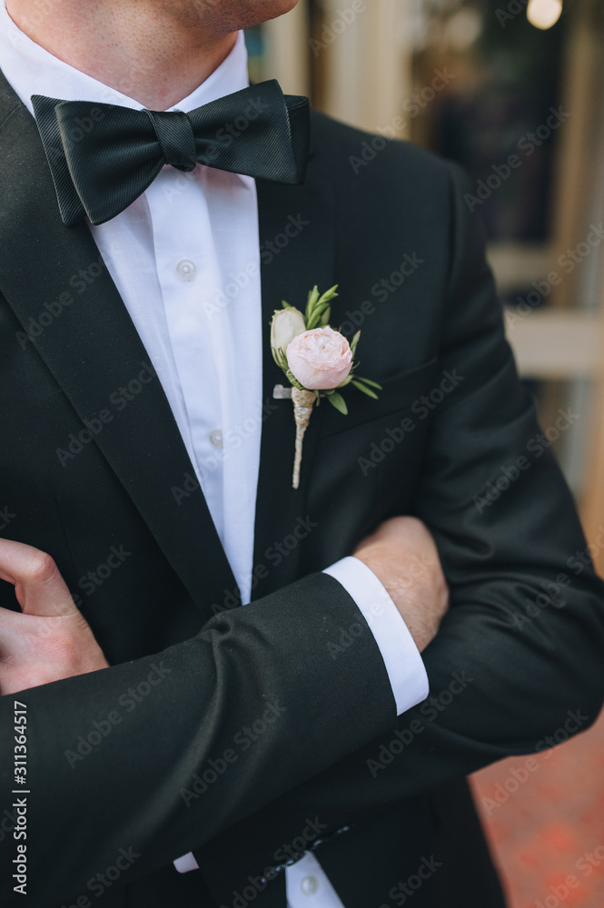 Wedding details of the groom close-up: Black suit, boutonniere, bow-tie ...