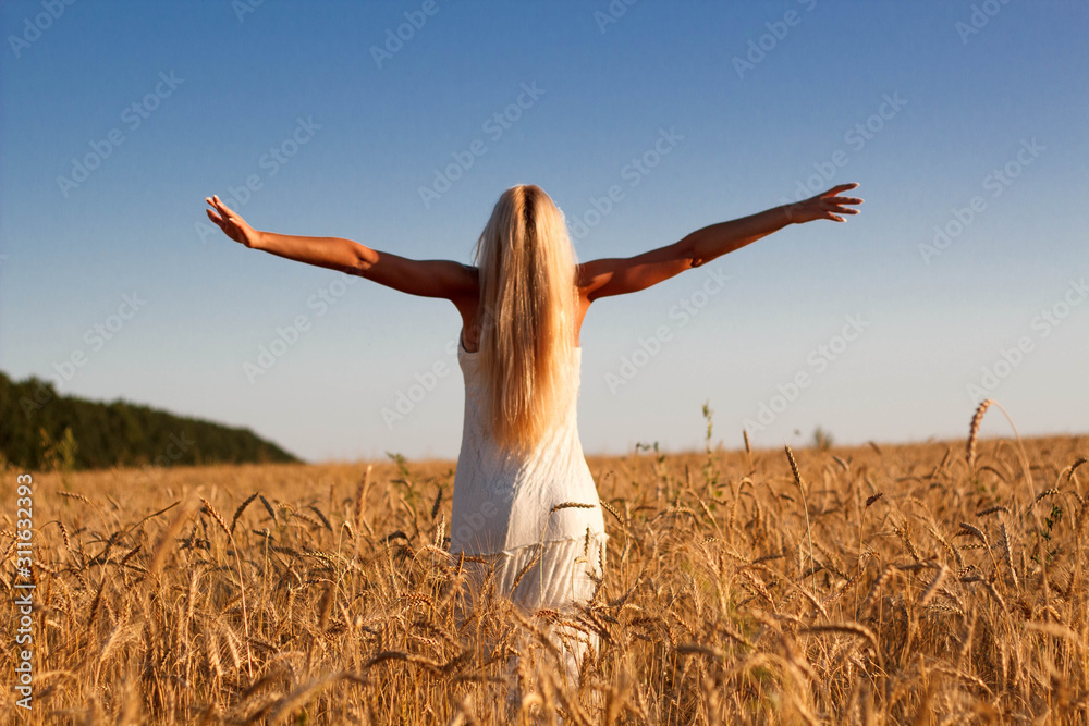 The girl stands with her back to the wheat field and looks up at the ...
