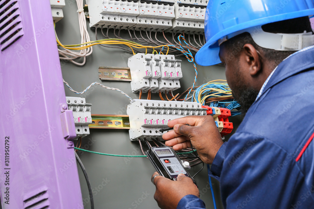 African-American electrician performing wiring in distribution board ...