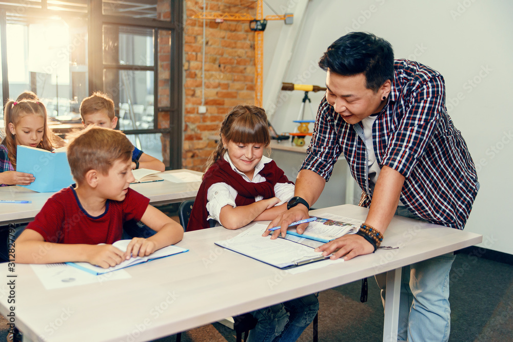Teacher helping school kids with test tasks in classroom at primary ...
