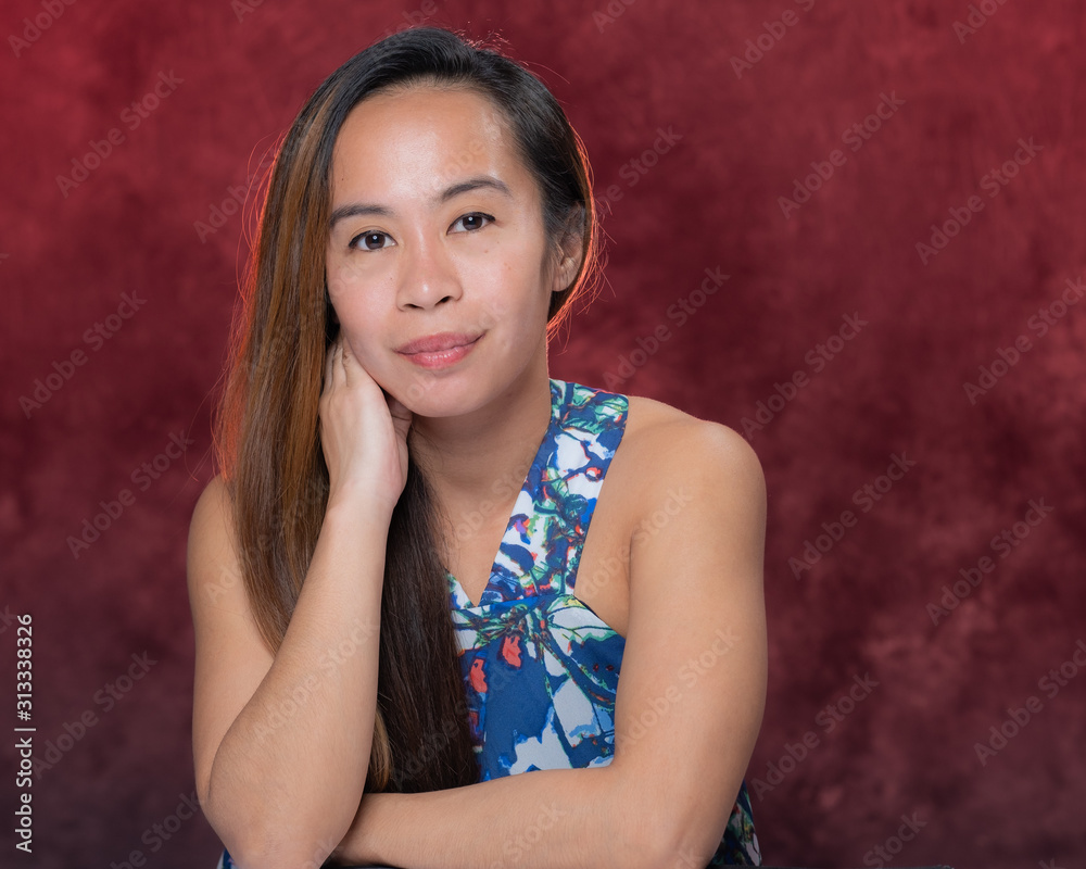 Young Filipina woman posing for studio headshots. Backlit on red and ...