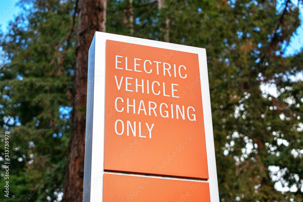 Electric vehicle charging only warning sign with blurred green trees in ...