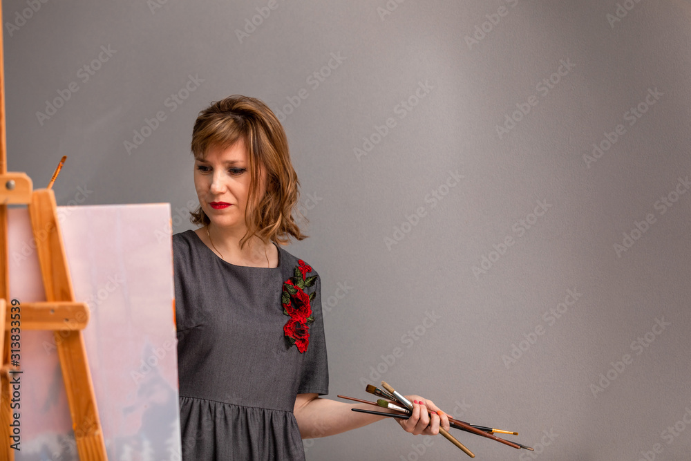 Portrait of a young artist girl who draws picture behind an easel. The ...