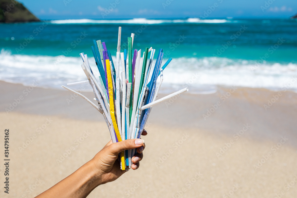 Hand holding heap of used plastic straws on background of clean beach ...