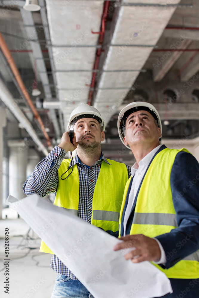 Male engineers flashlight blueprints looking up at construction site ...