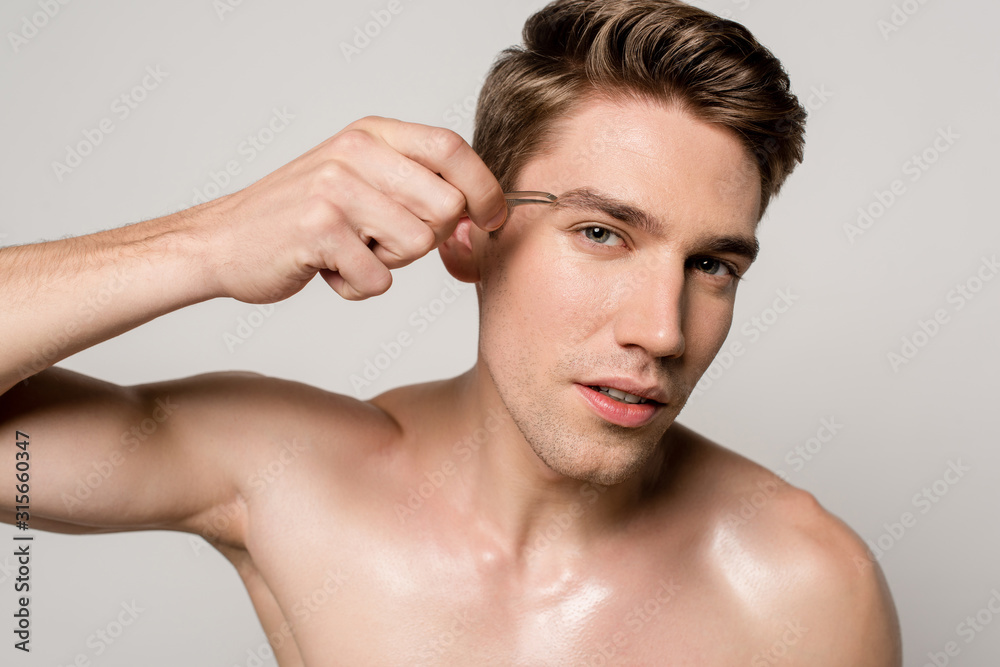 sexy man with bare torso pinching brows with tweezers isolated on grey ...
