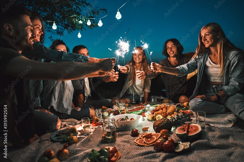 Happy friends having fun with fire sparkles. Young people camping at ...