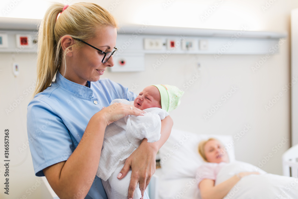 Young nurse standing in maternity ward and holding newborn baby in her ...