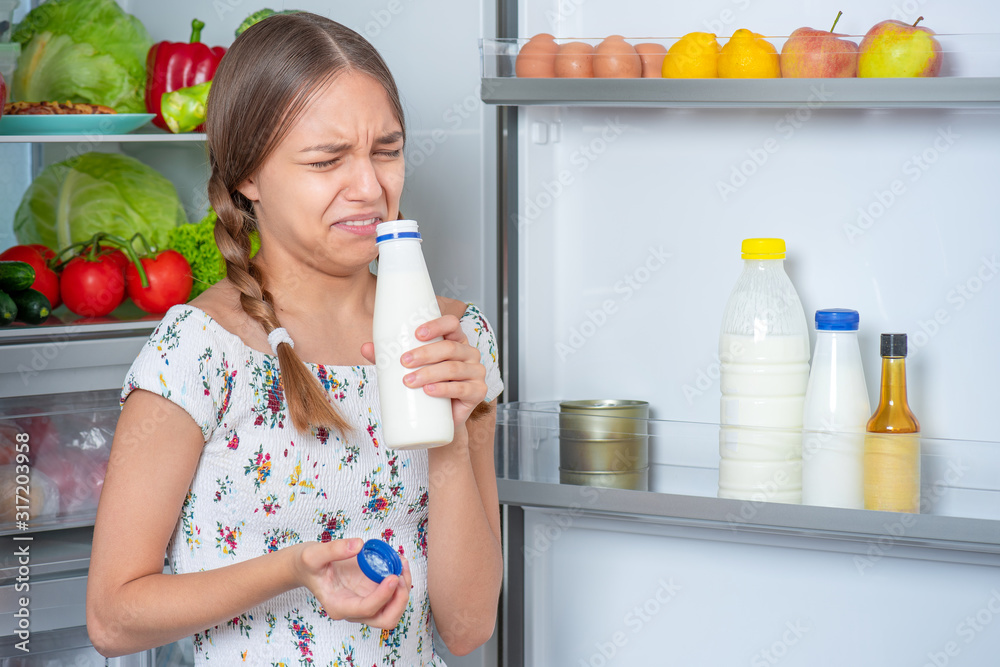 Beautiful young teen girl holding bottle of milk, sniffing with bad ...