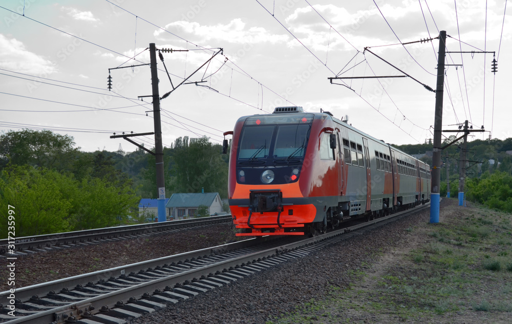New commuter train, colored in red and grey, goes by rail. A diesel ...
