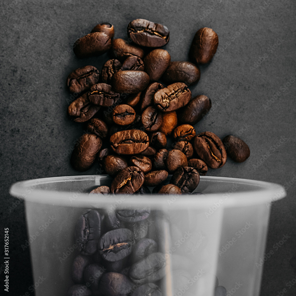 roasted coffee beans spill out of clear plastic glass onto an even ...