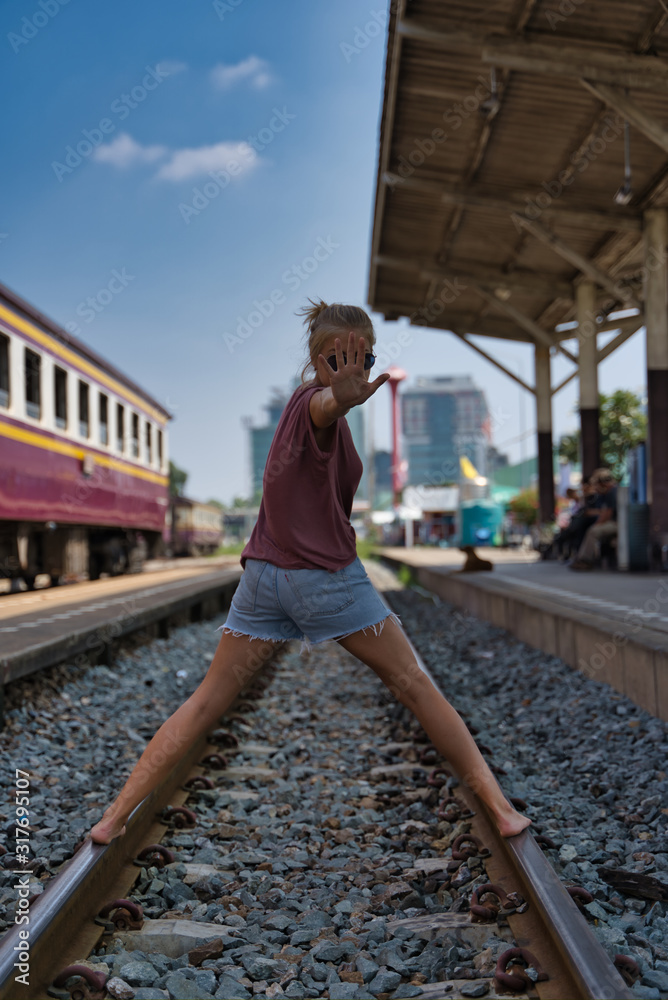 Blonde girl standing on a train track with her legs spread and one hand ...