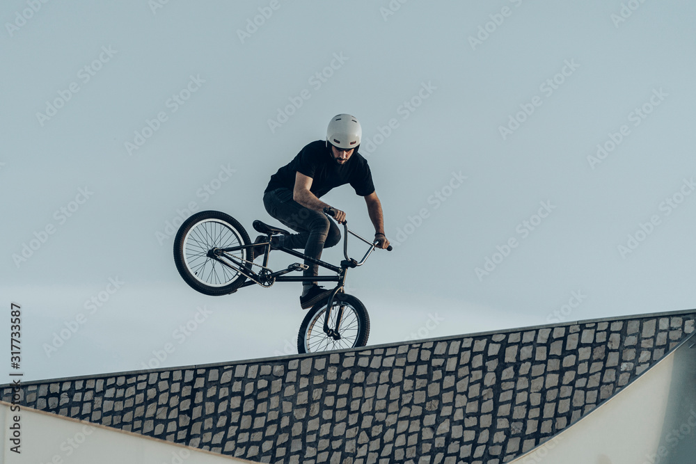 Bmx rider making a reversed wheelie on top of stone bricks bike park ...