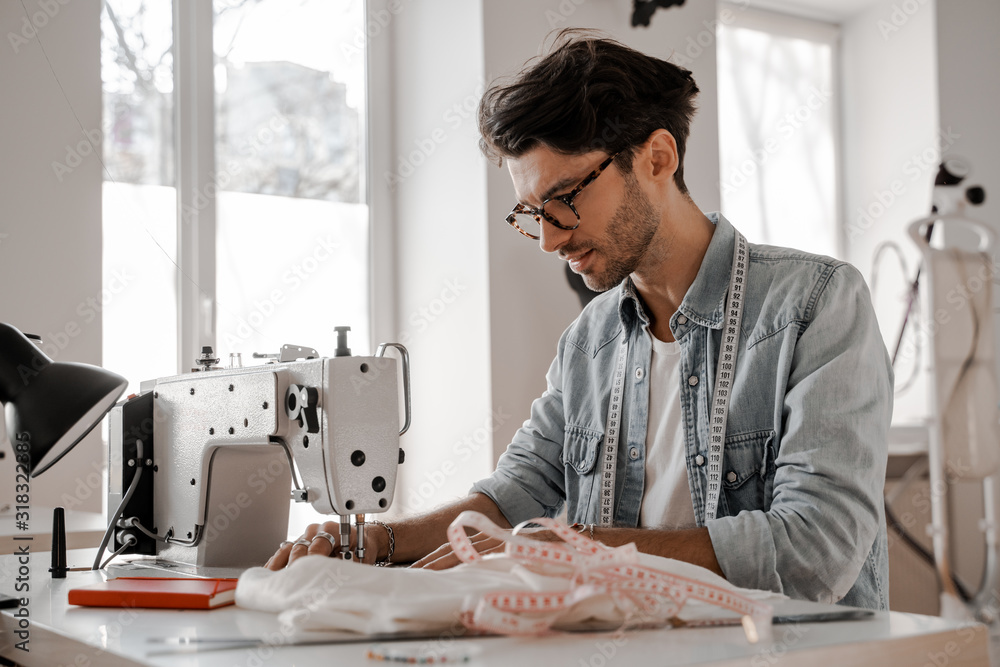 Stylish and fashionable clothes designer man sews at a sewing machine ...