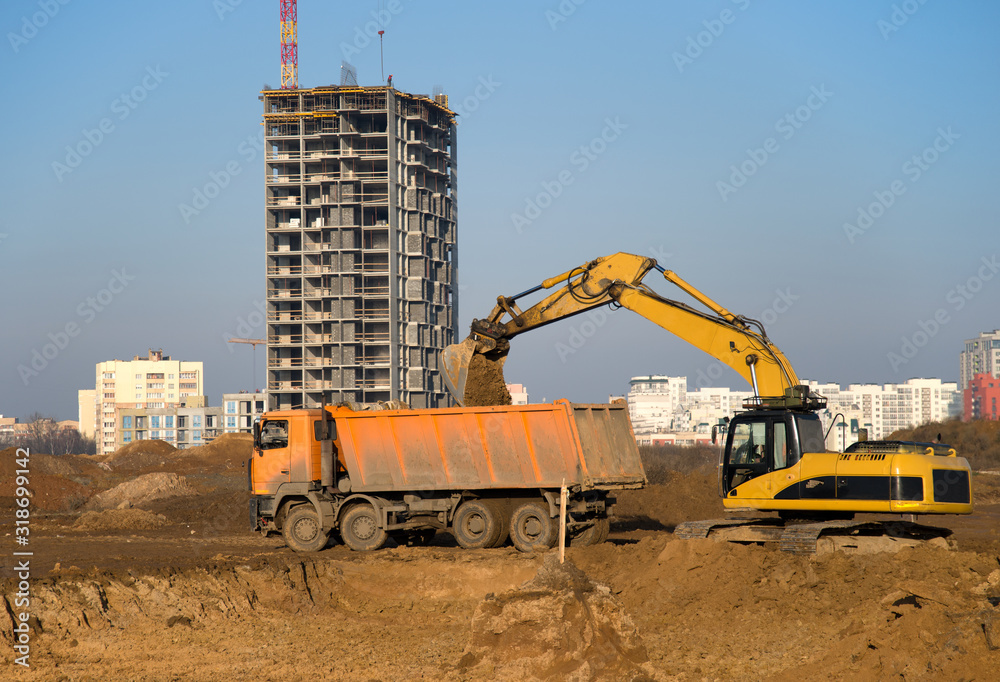 Excavator load the sand to the dump truck on construction site. Backhoe digs the ground for the ...
