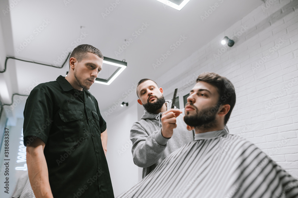 Photo Stock Two barbers cut a client with a beard at a men's ...