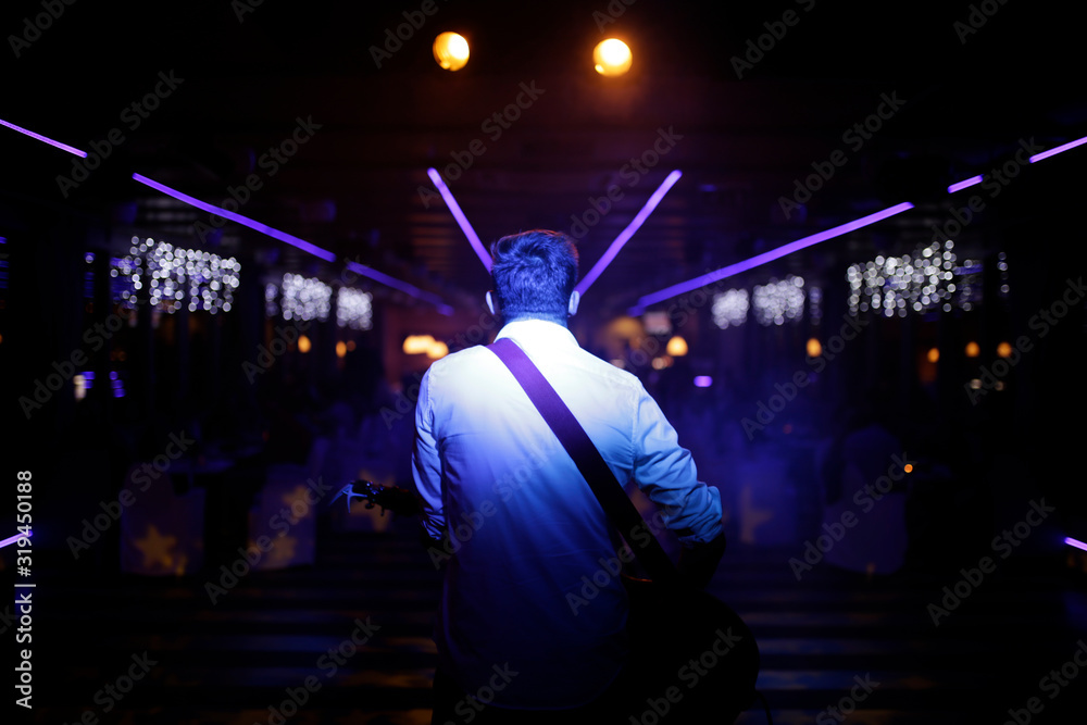 Singer with guitar at the stage. Back view ate the singer and podium ...